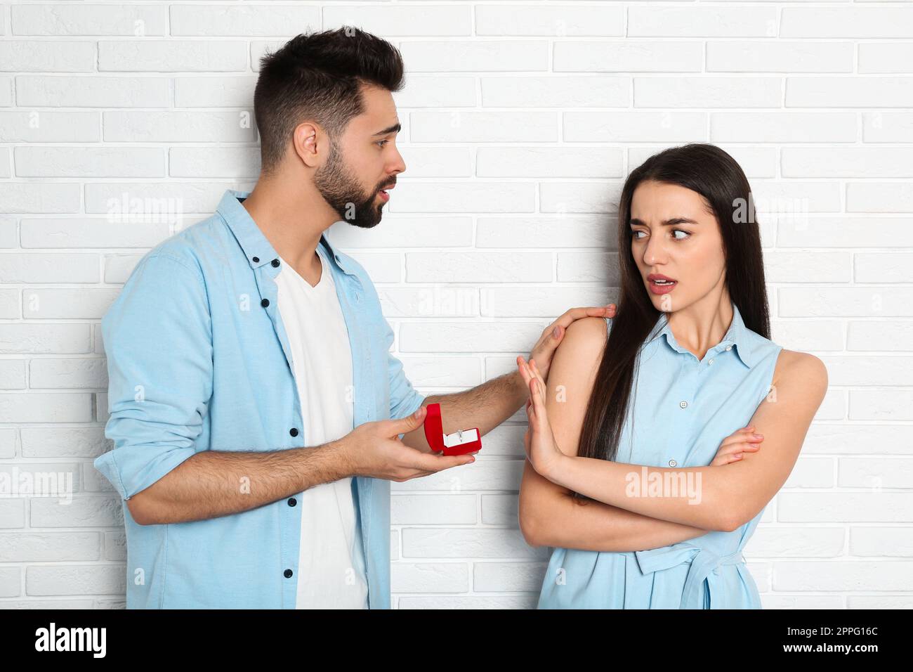 Young woman rejecting engagement ring from boyfriend near white brick ...