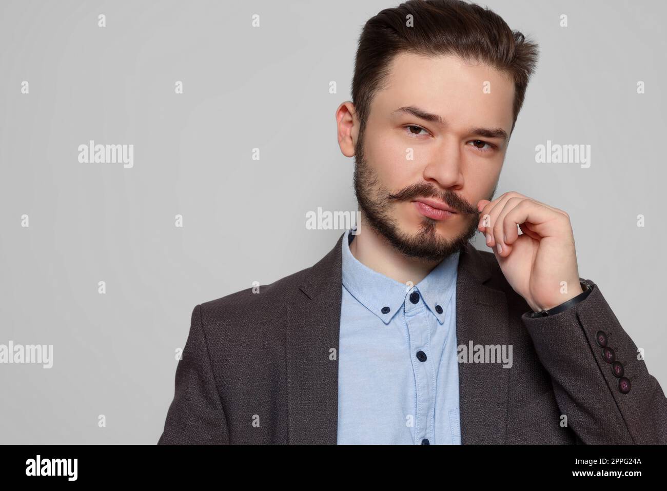 Handsome man in suit touching mustache on light grey background. Space ...
