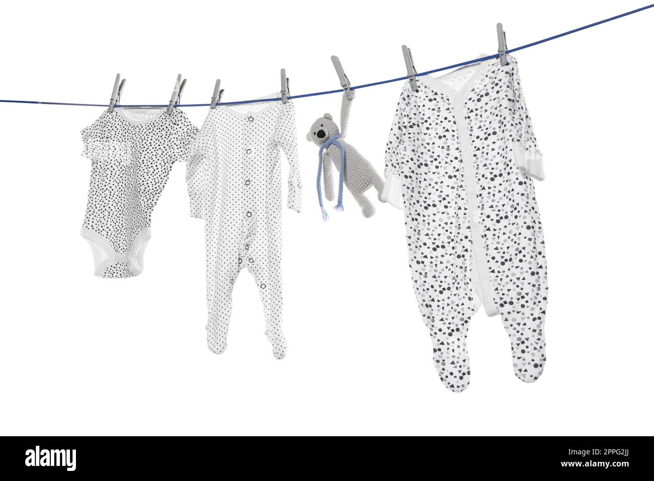Different baby clothes and toy drying on laundry line against white ...