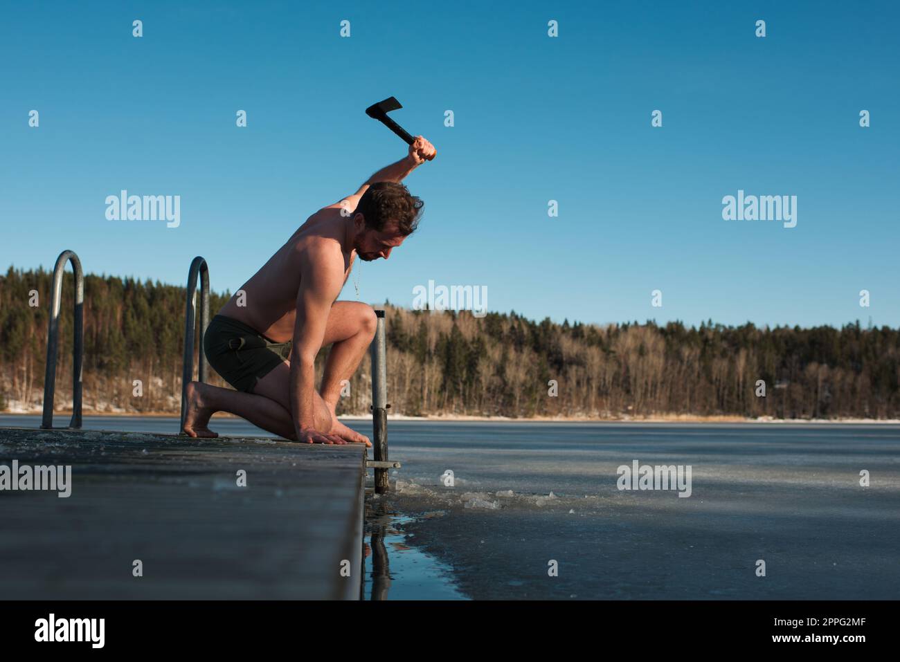 Man using an axe to break the ice in the sea to go cold water swimming ...