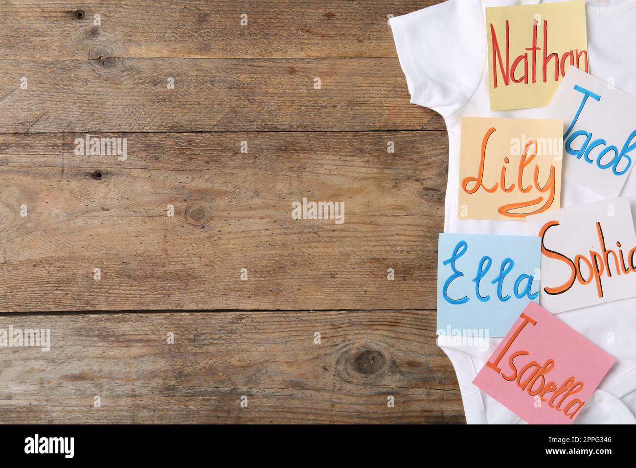 Paper notes with different baby names and child's bodysuit on wooden ...