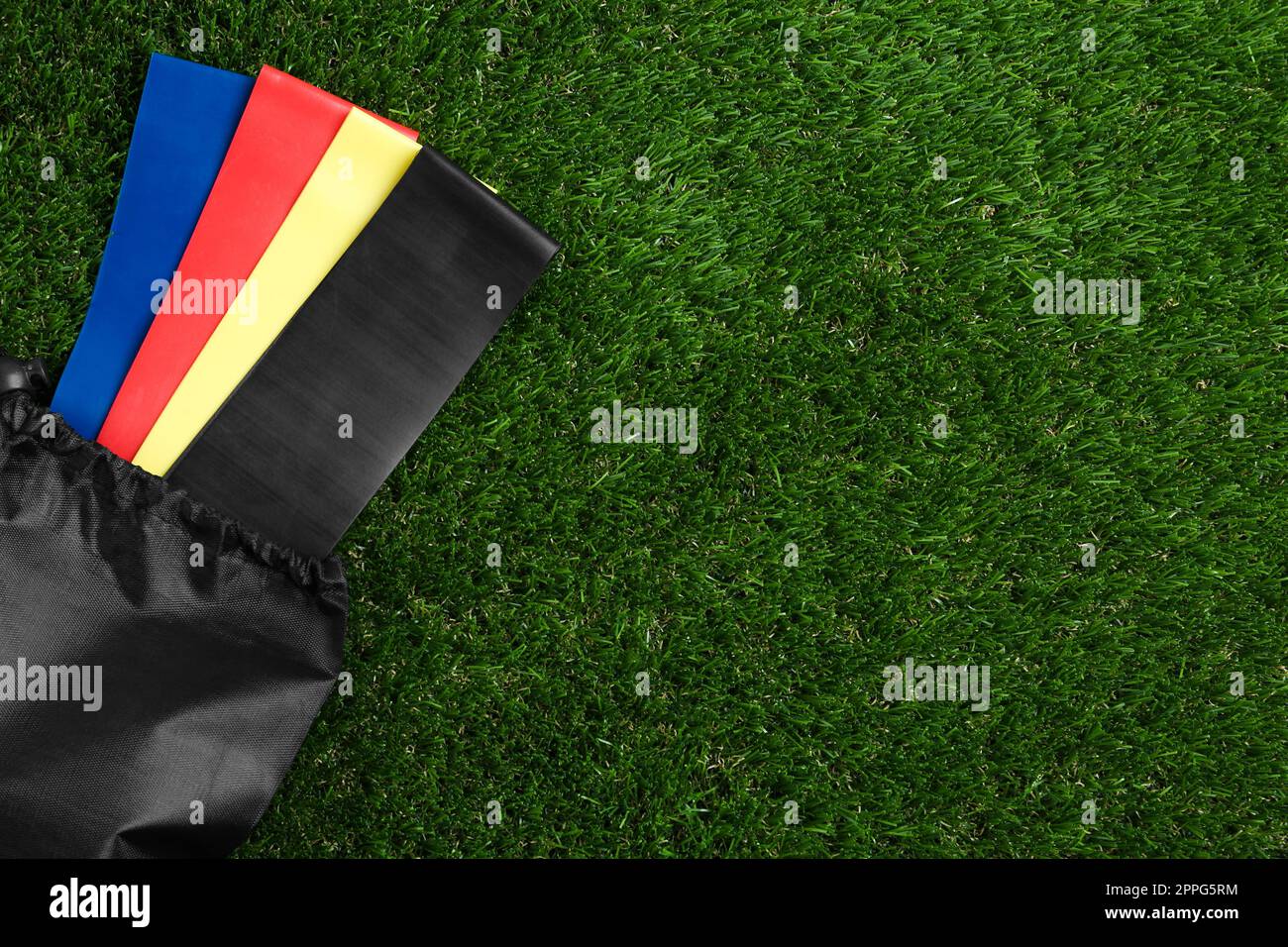 Bag with fitness elastic bands on green grass, top view. Space for text ...