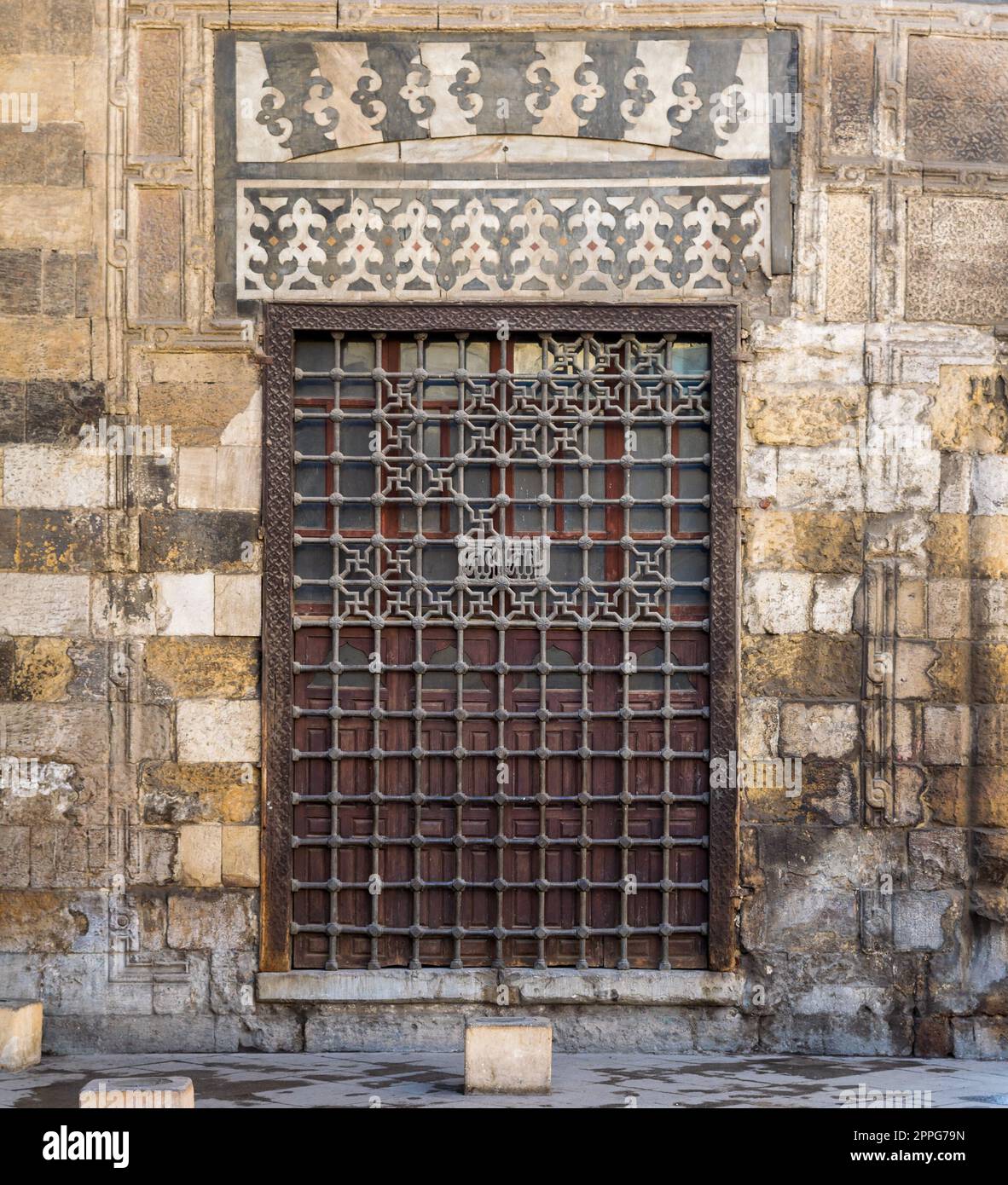 Wooden grunge window with decorated iron grid over stone bricks wall ...