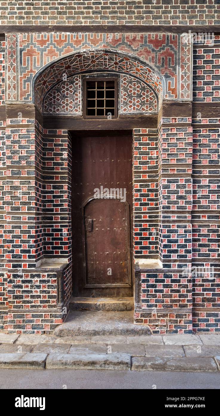 Wooden grunge decorated arched gate with inner small door on wall with ...