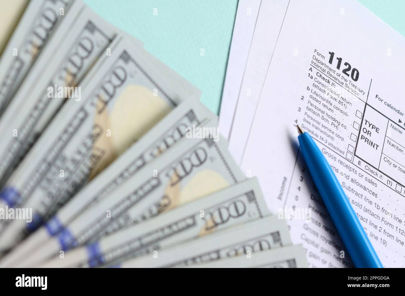 1120 tax form lies near hundred dollar bills and blue pen on a light ...