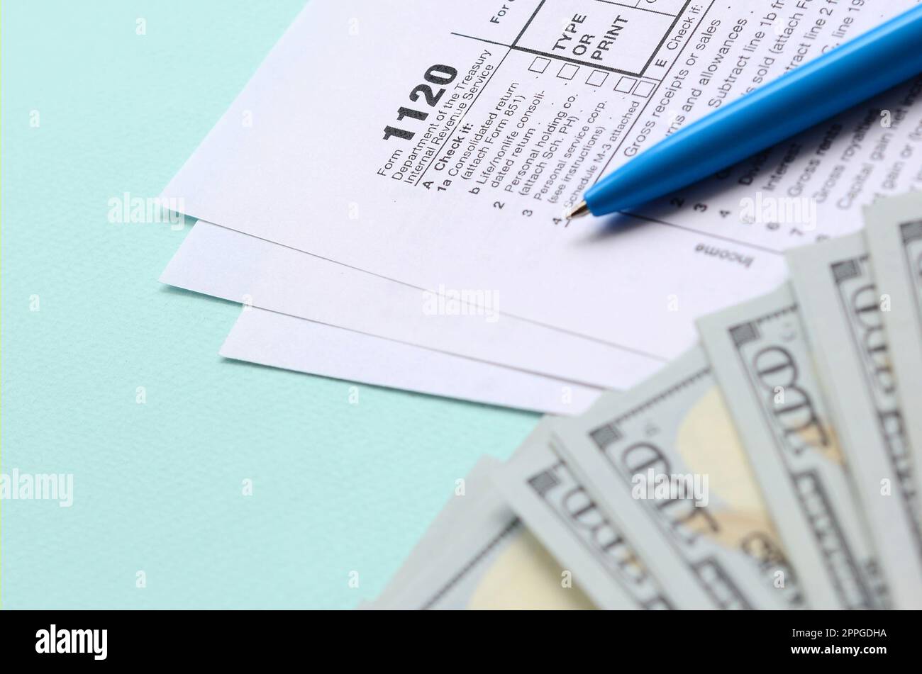 1120 tax form lies near hundred dollar bills and blue pen on a light blue background. US ...