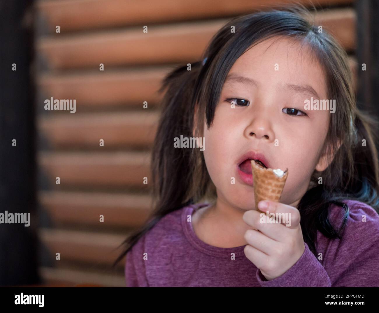 Little Asian girl eating ice cream, wood shade stripes background Stock ...