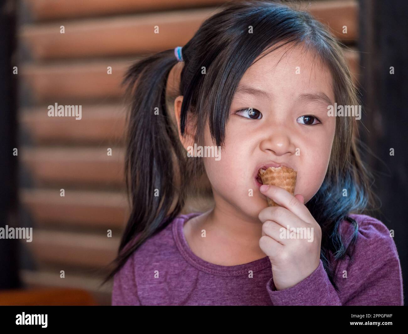 Little Asian girl eating ice cream, wood shade stripes background Stock ...