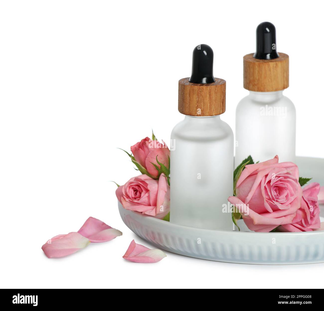Bottles of essential rose oils and flowers on plate against white ...