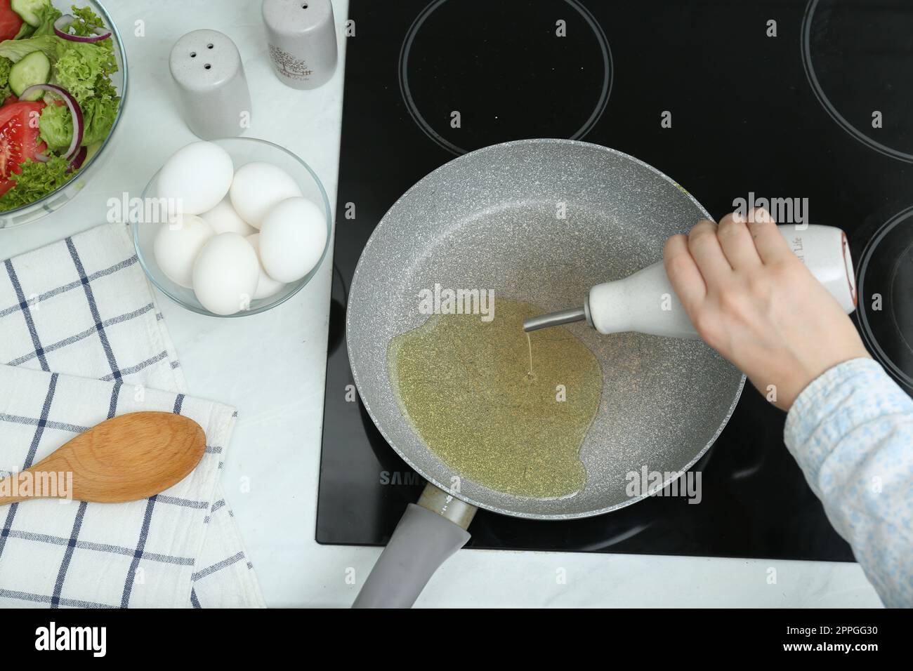 Woman pouring cooking oil from bottle into frying pan in kitchen, top ...