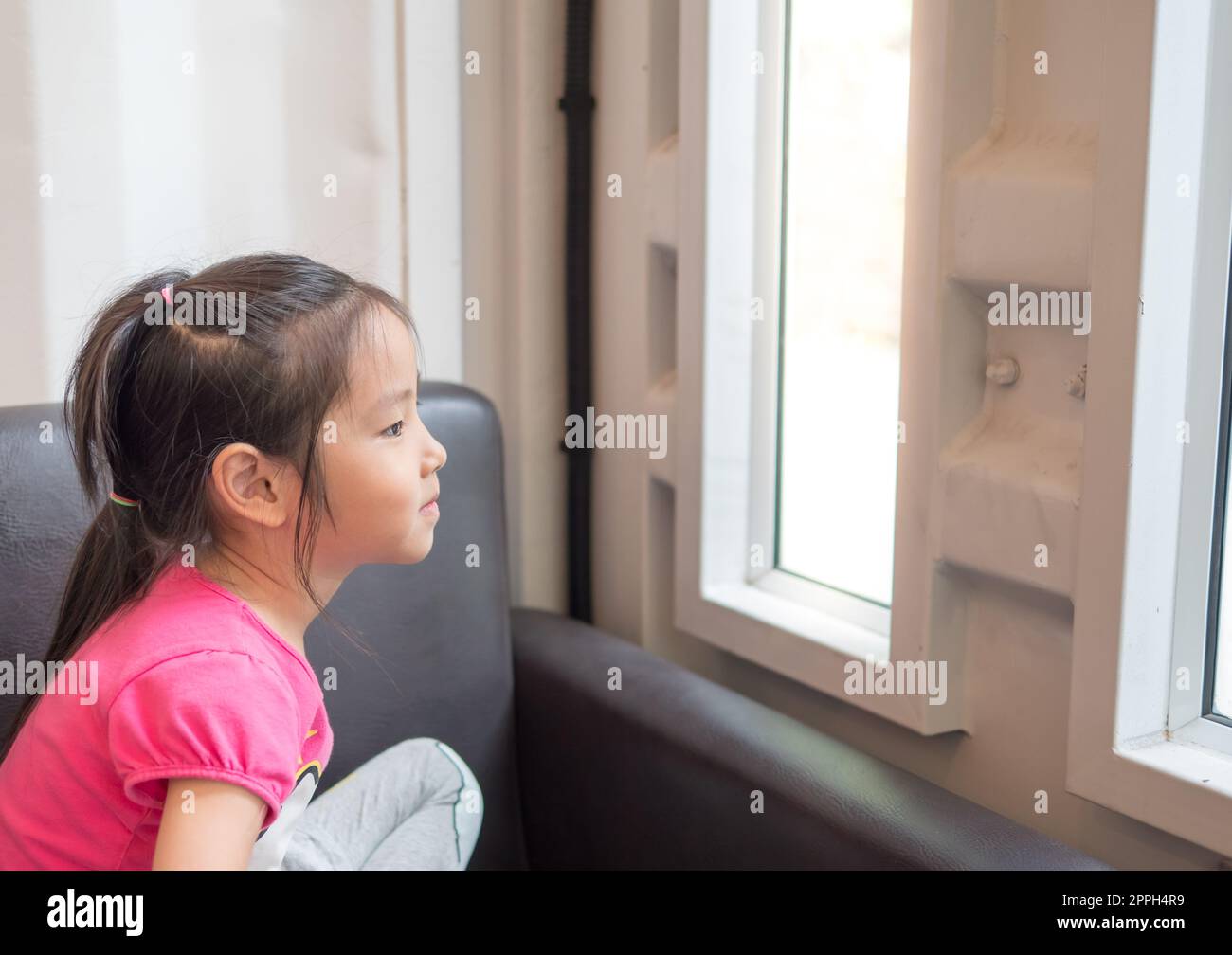Beautiful little girl watching out the window. sit on the sofa Stock ...