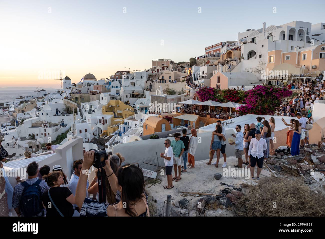 Whitewashed houses and windmills in Oia in warm rays of sunset on ...