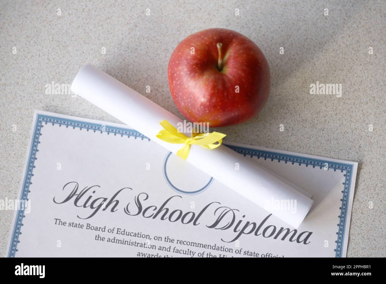 A high school diploma lies on table with small scroll and red apple ...