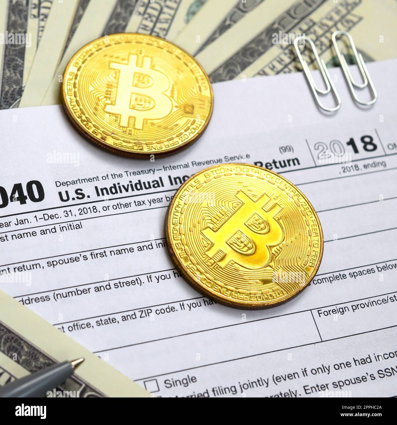 The pen, bitcoins and dollar bills is lies on the tax form 1040 U.S ...