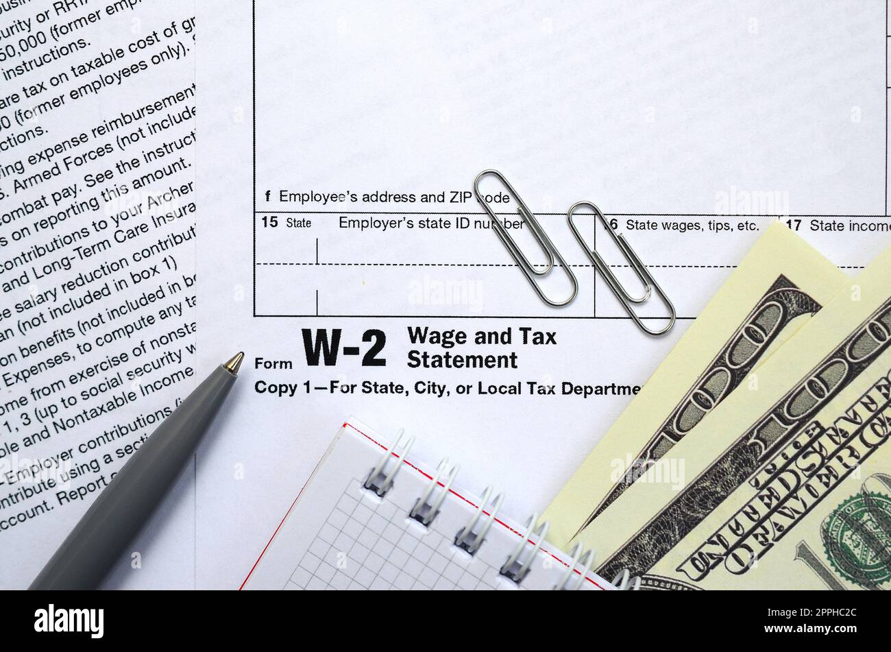 The pen, notebook and dollar bills is lies on the tax form W-2 Wage and ...