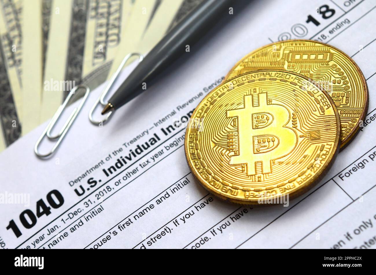 The pen, bitcoins and dollar bills is lies on the tax form 1040 U.S ...