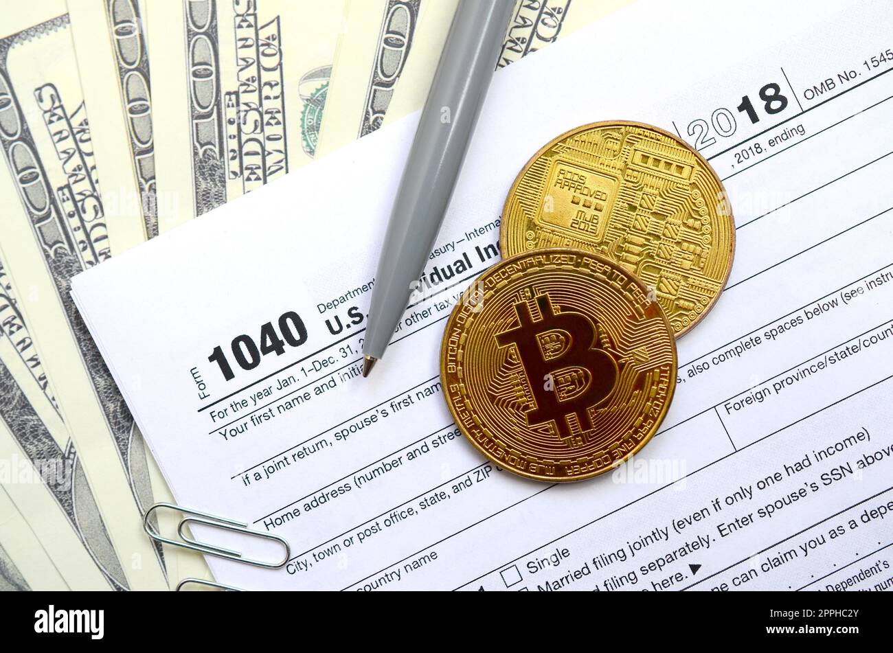 The pen, bitcoins and dollar bills is lies on the tax form 1040 U.S ...
