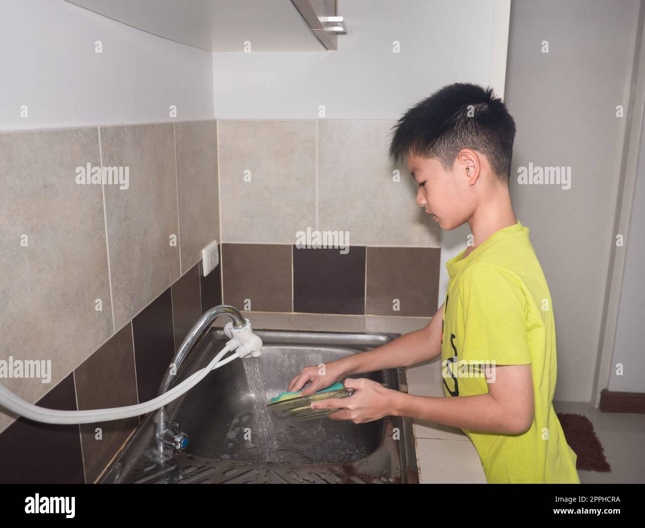 Adorable kid boy washing dishes in domestic kitchen. Child having fun with helping his parents ...