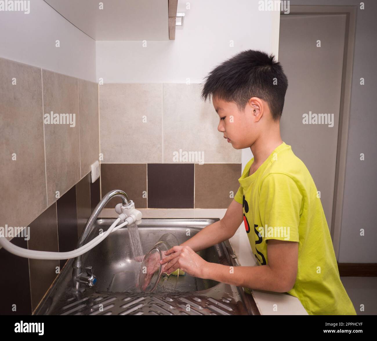 Adorable kid boy washing dishes in domestic kitchen. Child having fun with helping his parents ...