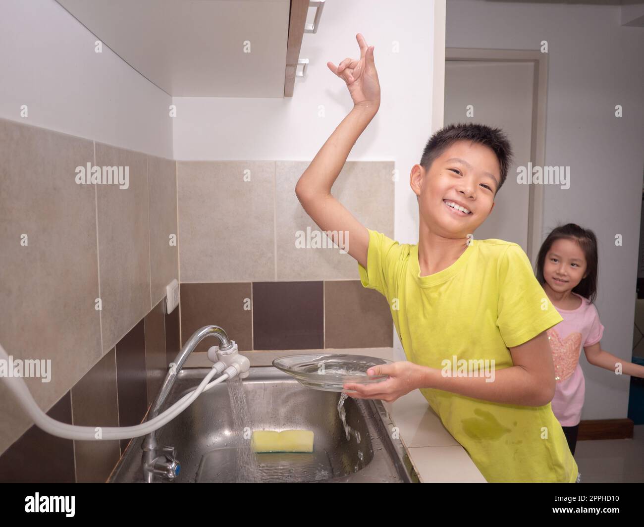 Adorable kid boy washing dishes in domestic kitchen. Child having fun with helping his parents ...
