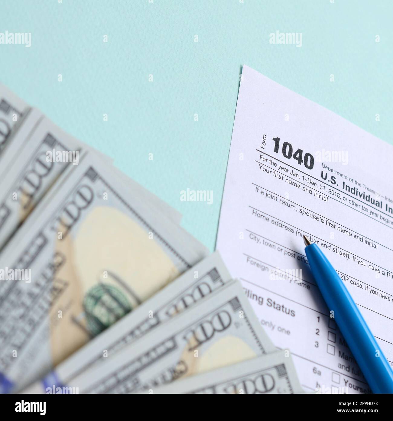 1040 tax form lies near hundred dollar bills and blue pen on a light blue background. US ...