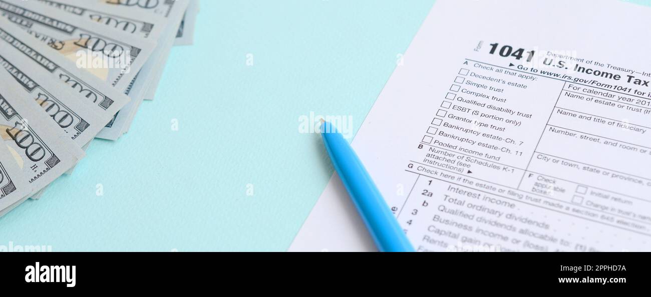 1041 tax form lies near hundred dollar bills and blue pen on a light ...