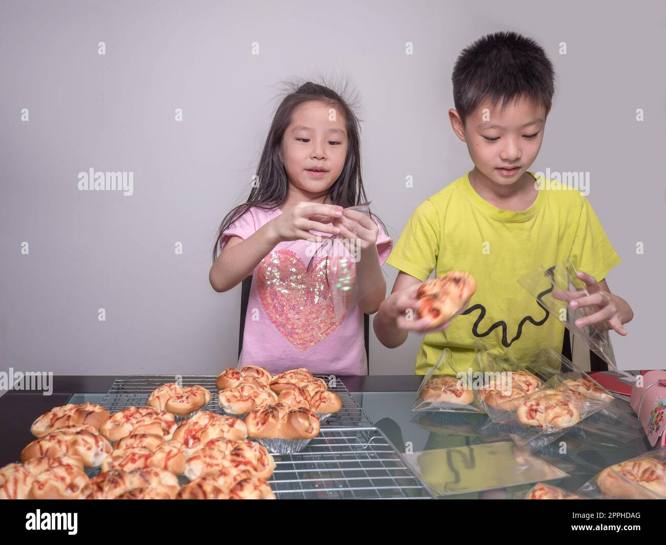 Adorable kid girl and boy separate packing baked pork sausage with ...