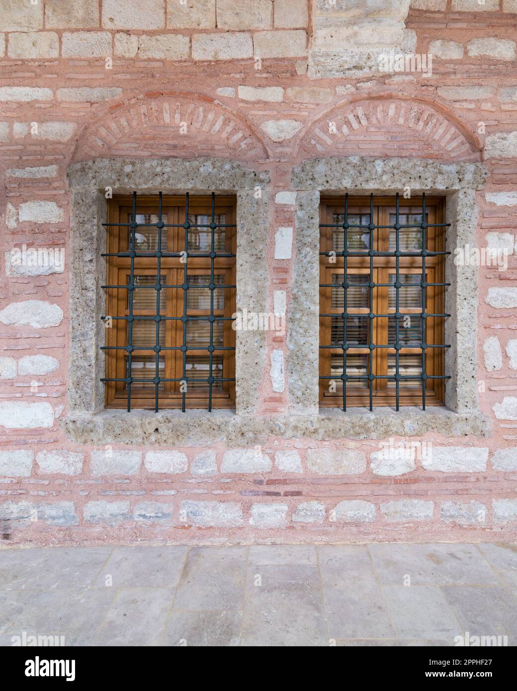Two adjacent wooden arched windows in a red and white stone bricks wall ...