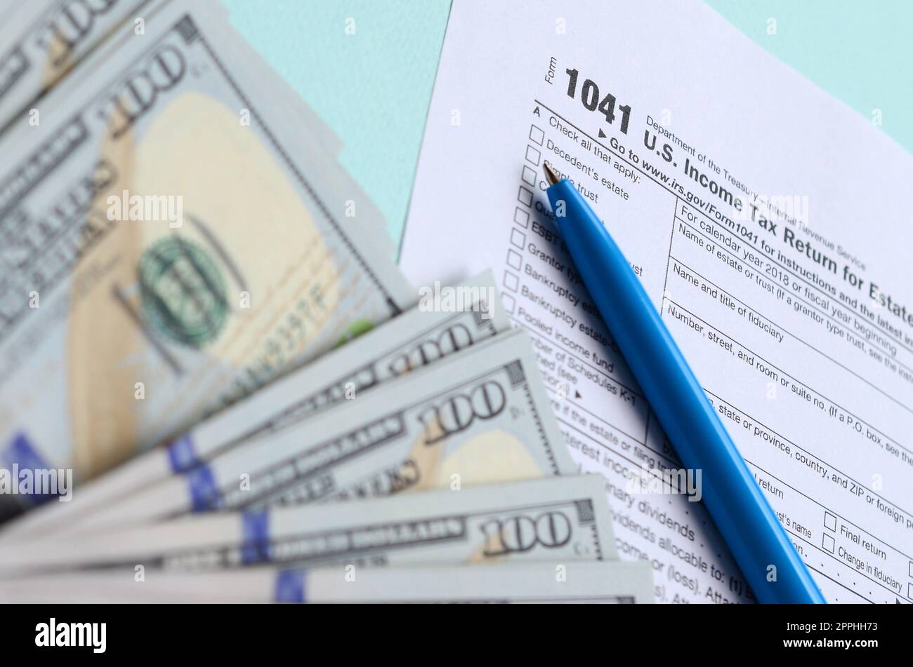 1041 tax form lies near hundred dollar bills and blue pen on a light ...