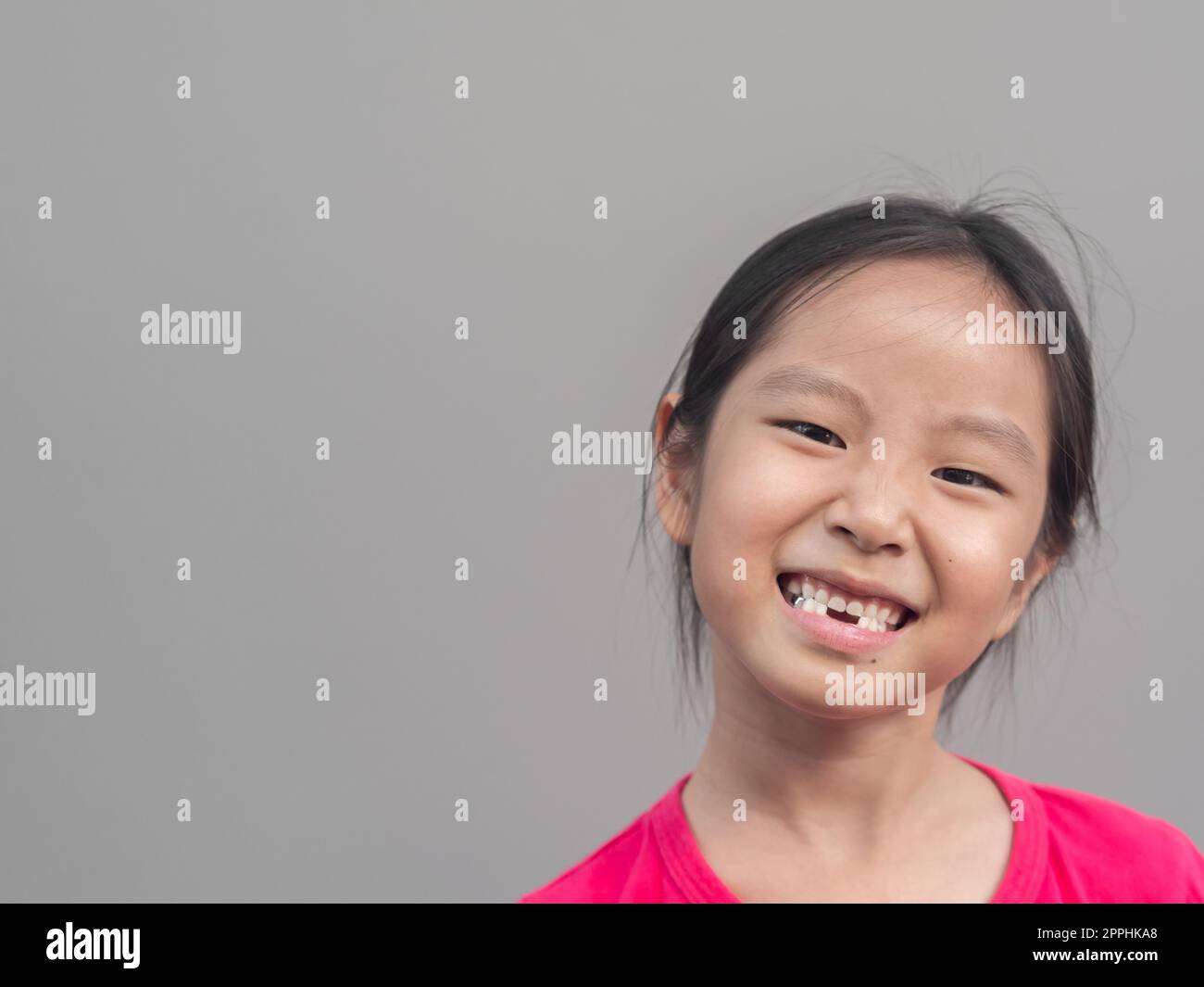 Asian little cute girl smile with her broken tooth , grey background ...