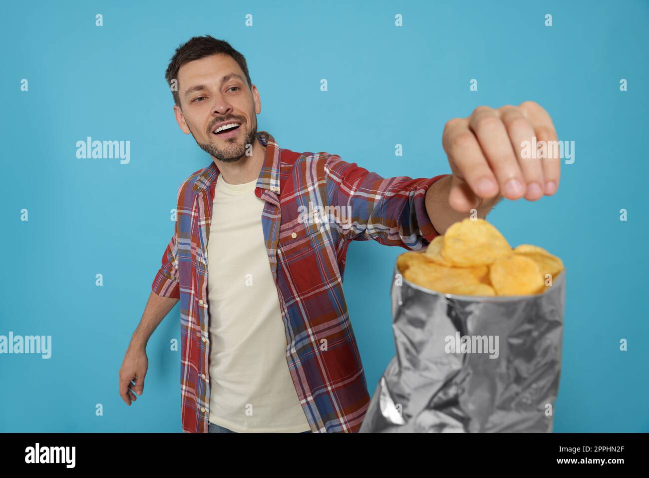 Handsome man eating potato chips on light blue background Stock Photo ...