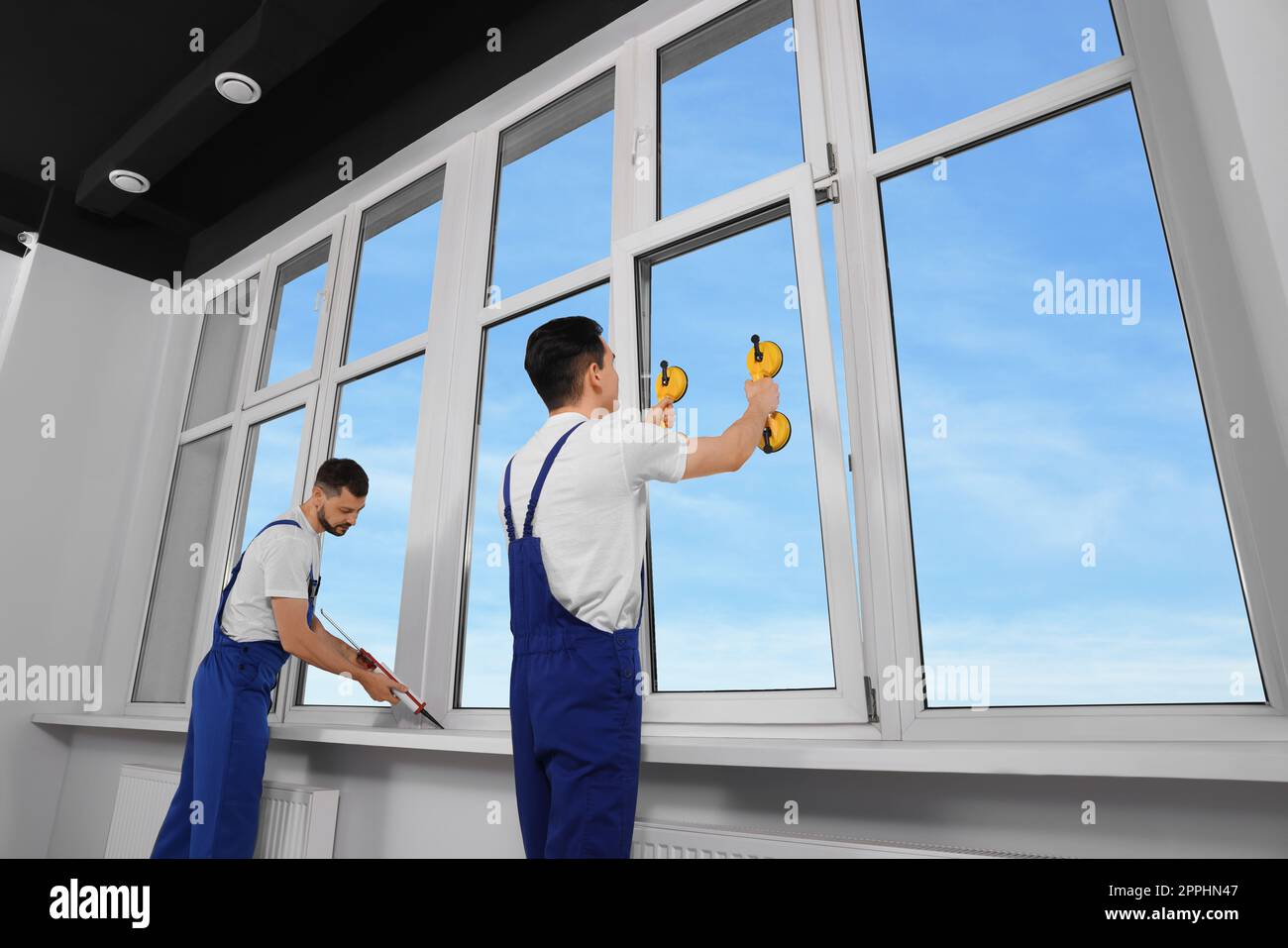 Workers with tube of sealant and suction lifters installing plastic ...