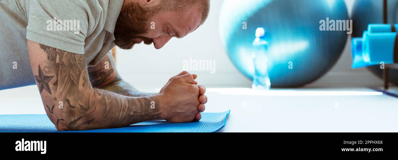 Muscled tattooed man leaning on a blue mat in the gym, doing push-ups ...