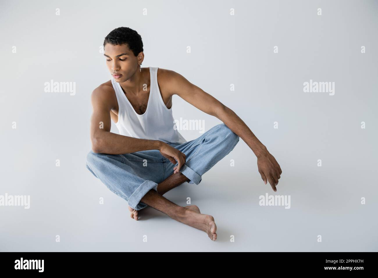 barefoot african american man in jeans sitting with crossed legs on ...