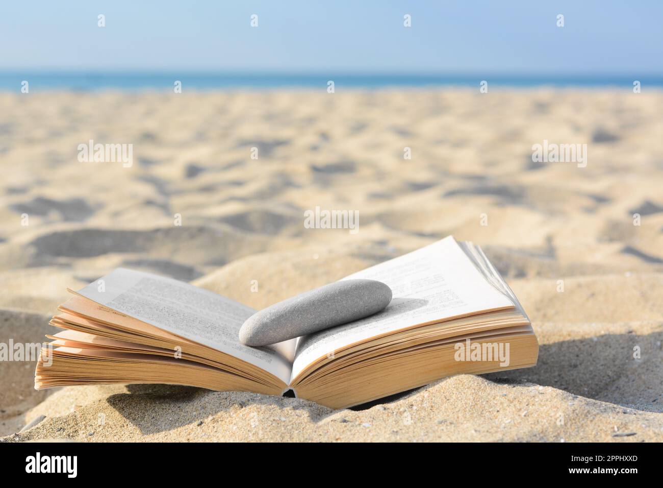 Open book with stone on sandy beach near sea, space for text Stock ...