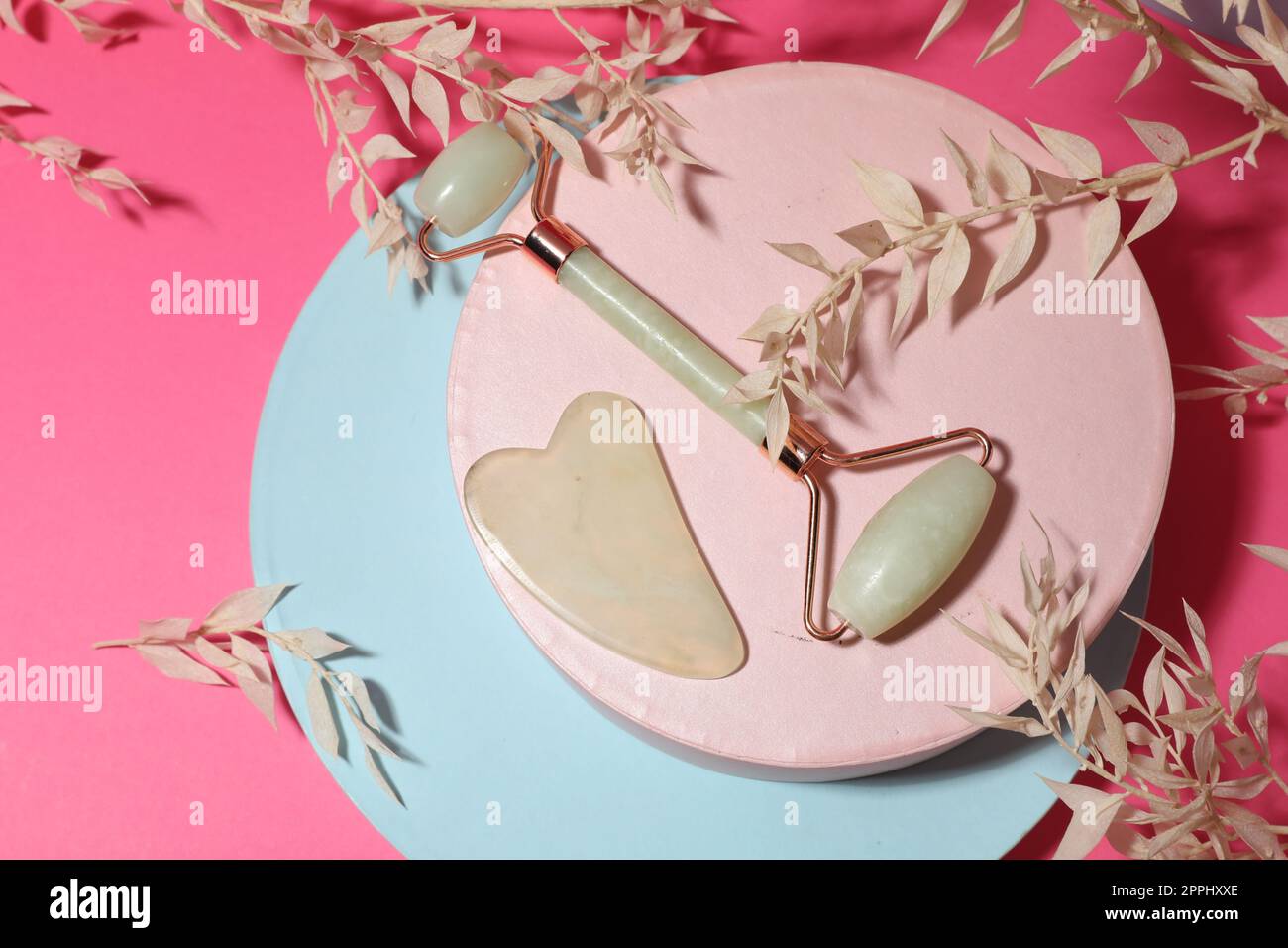 Flat lay composition with gua sha stone and face roller on pink ...