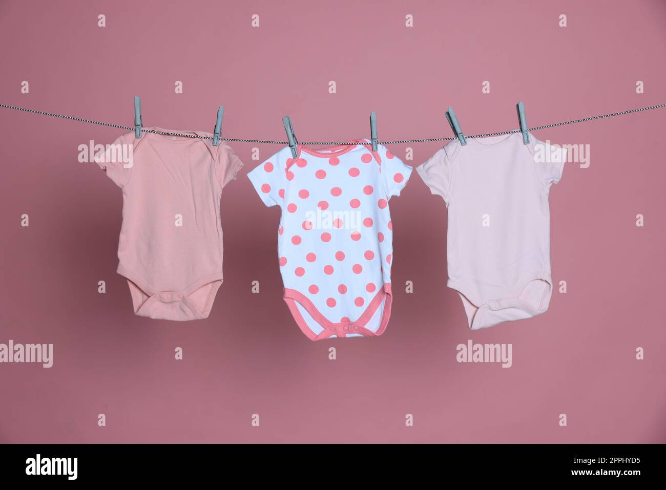 Baby clothes drying on laundry line against pink background Stock Photo ...