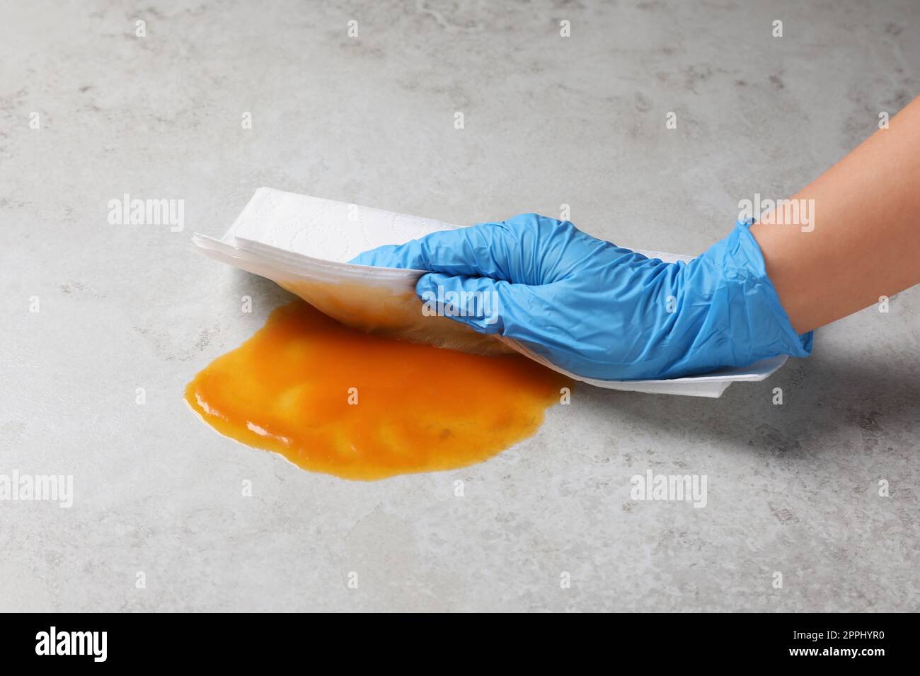 Woman wiping spilled sauce with paper towel on grey surface, closeup ...