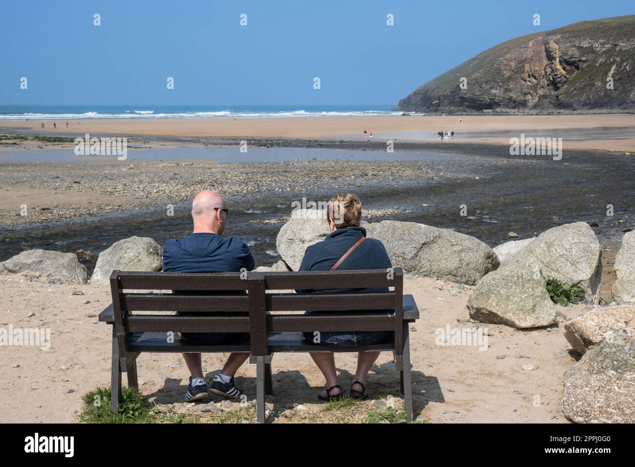Holidaymakers sitting together on a bench looking out over Mawgan beach ...