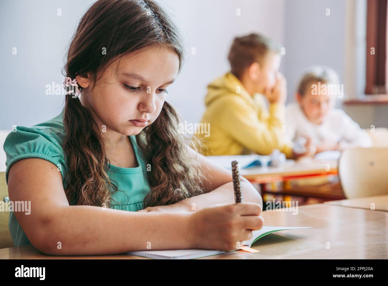 Young sad focused girl doing her homework during classes at school ...