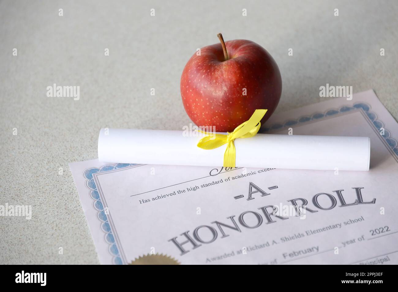A honor roll lies on table with small scroll and red apple. Education ...