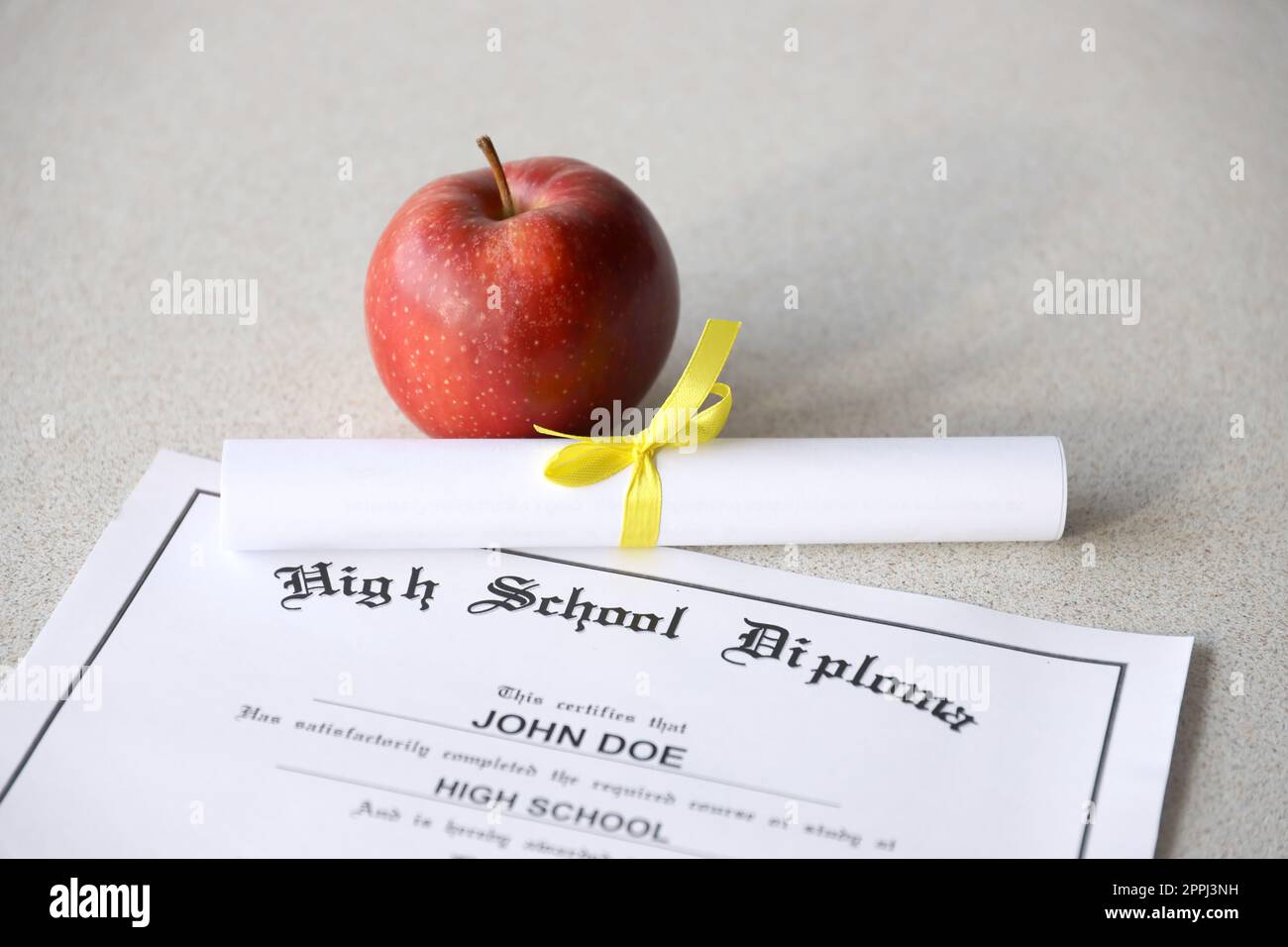 A high school diploma lies on table with small scroll and red apple ...