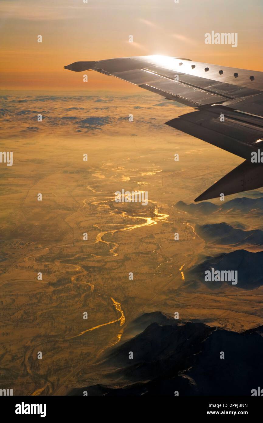 Wing of commercial airplane over asian winter landscape with orange ...