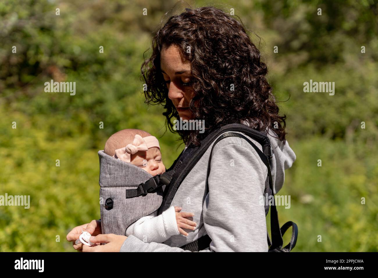 Young mom walking while carrying her newborn baby in an ergonomic ...