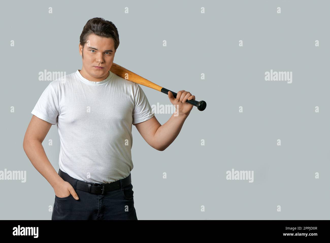 A stylish man holds a bat on his shoulder on a gray isolated background ...