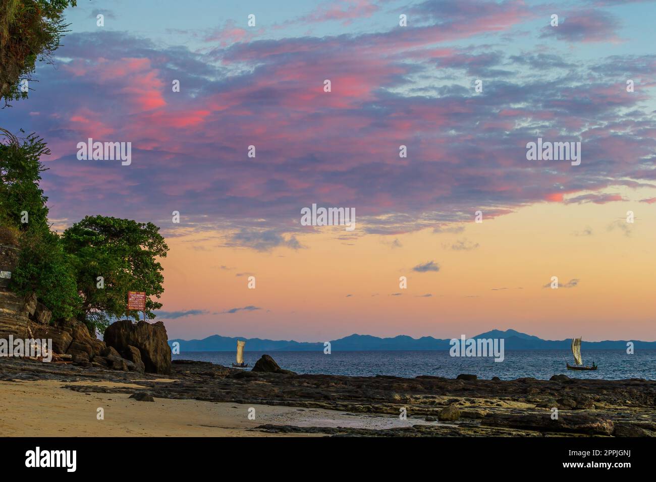View of coastline on Nosy Komba Island lined with palm trees and boats ...