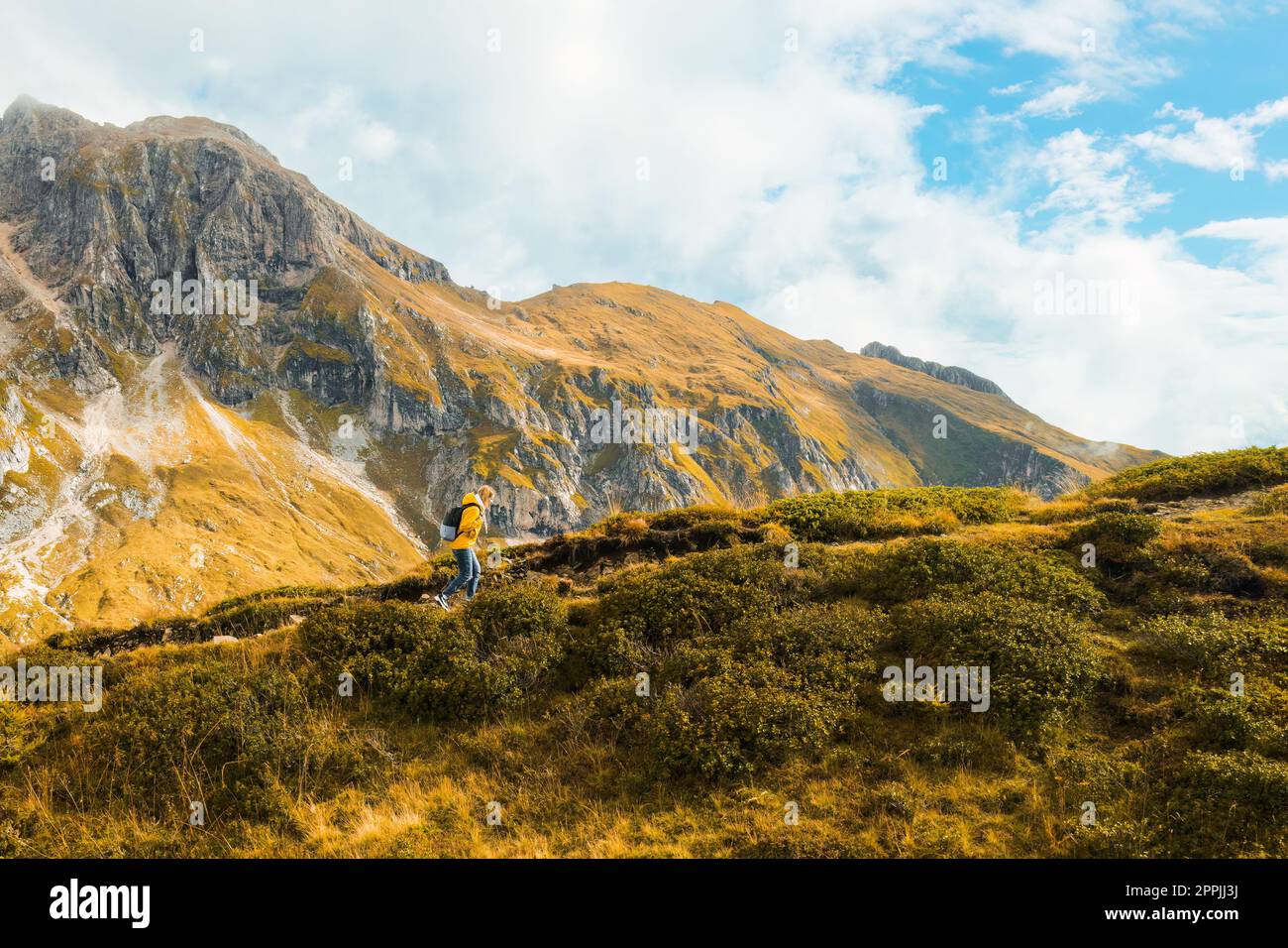 Woman tourist in yellow jacket walks on mountain top edge in Dolomites ...