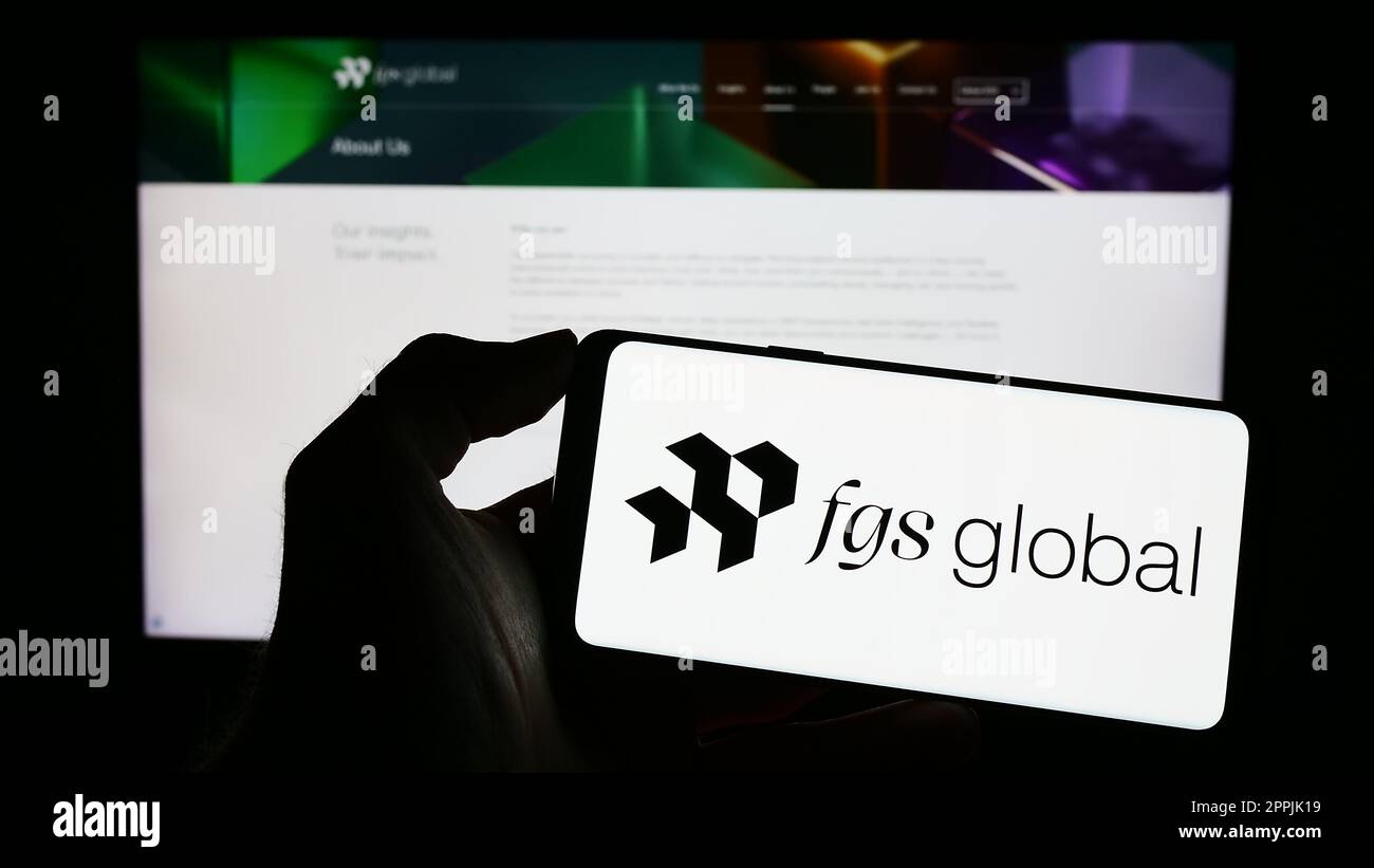 Person holding cellphone with logo of US public relations company FGS ...