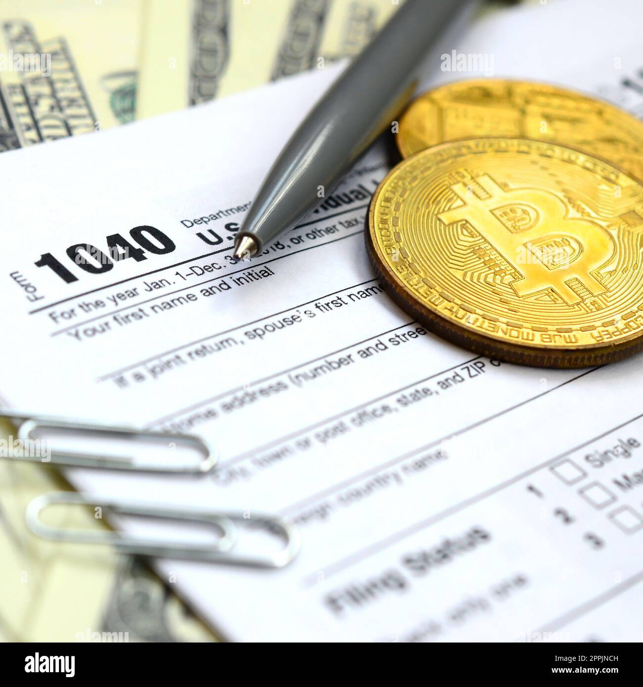 The pen, bitcoins and dollar bills is lies on the tax form 1040 U.S ...
