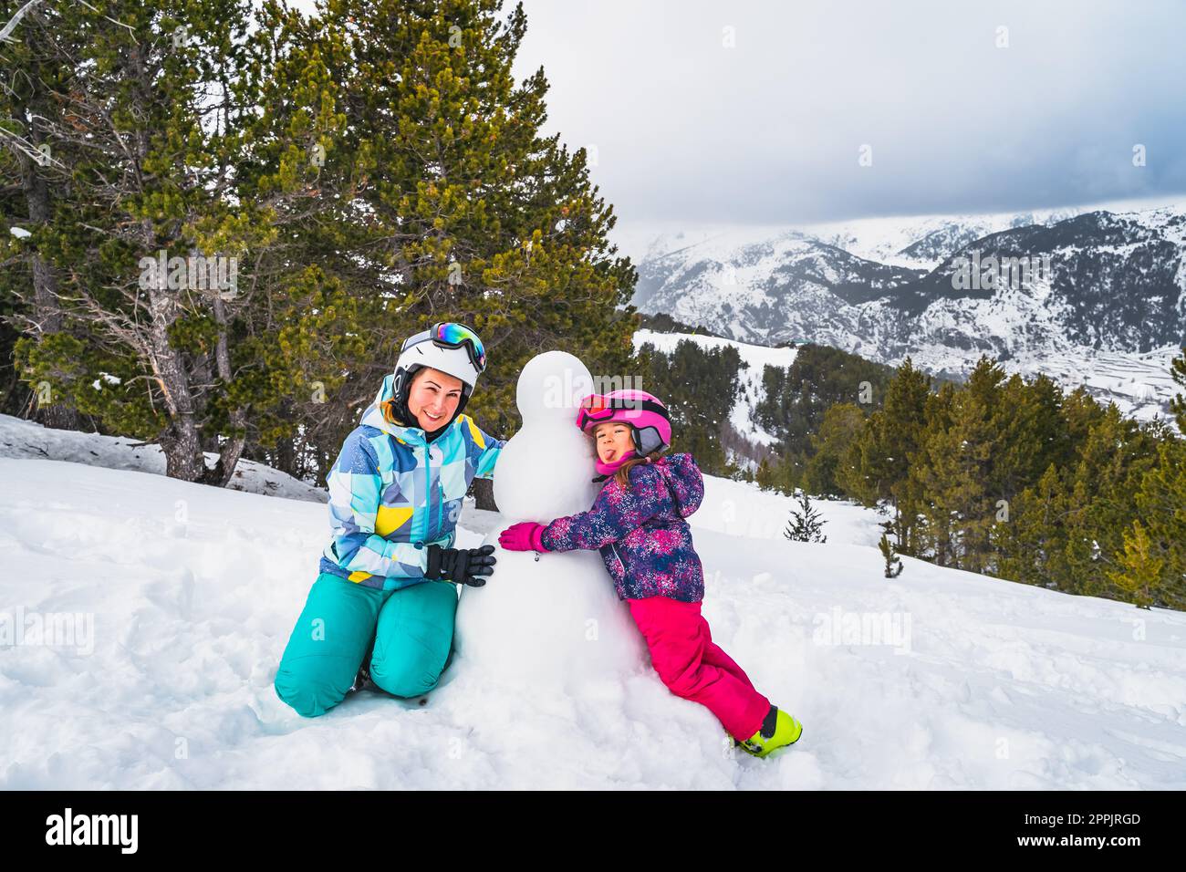 Mother and daughter hugging snowman. Ski winter holidays in Andorra ...